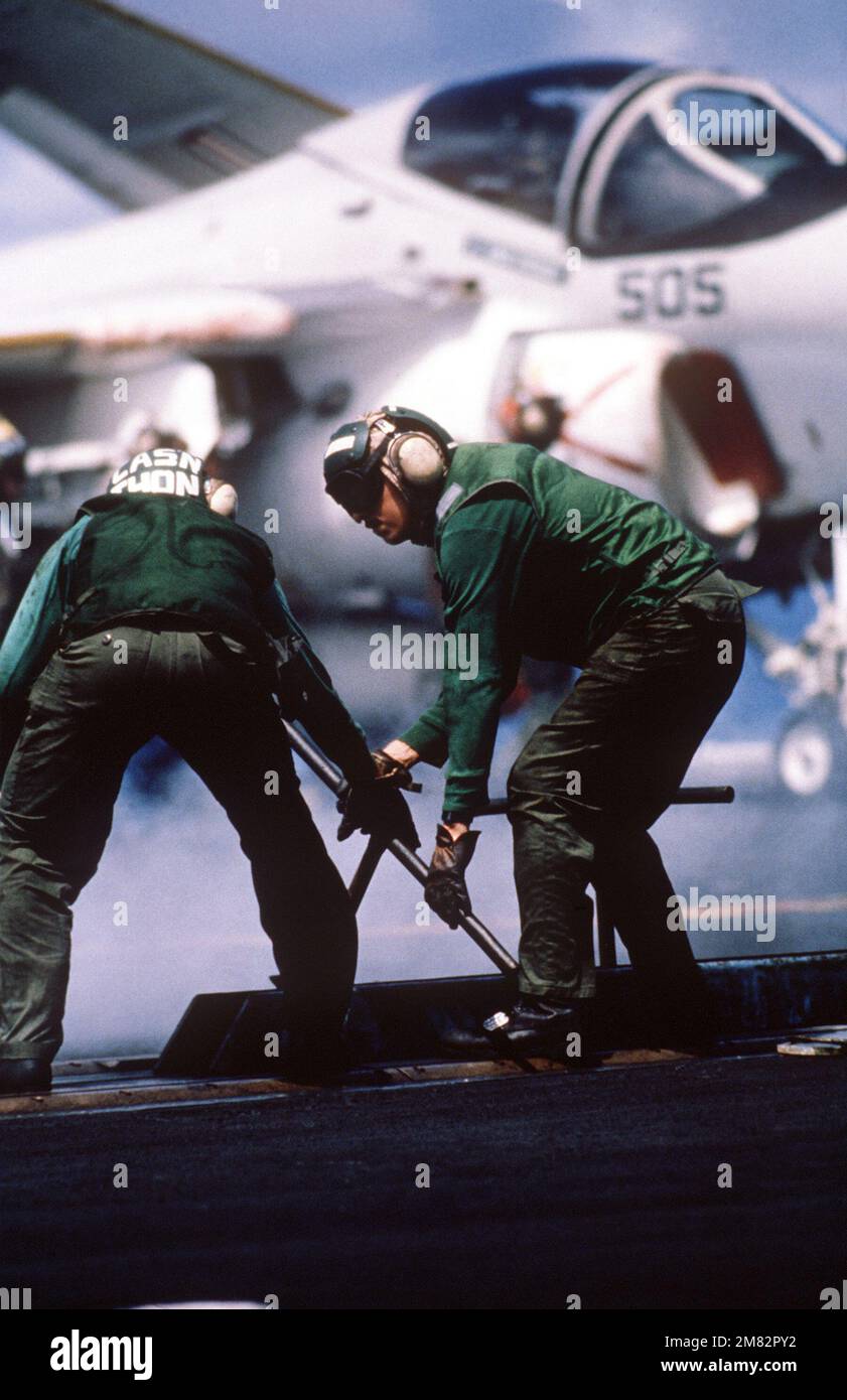Two catapult crewmen position an A-6 Intruder aircraft shuttle with a ...