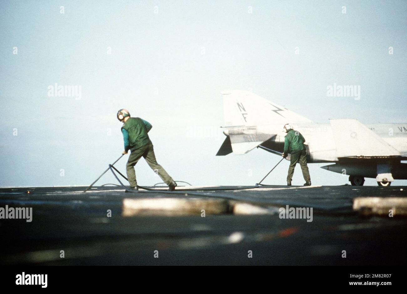 Two green-shirted bar runners guide the arresting cable as it is ...