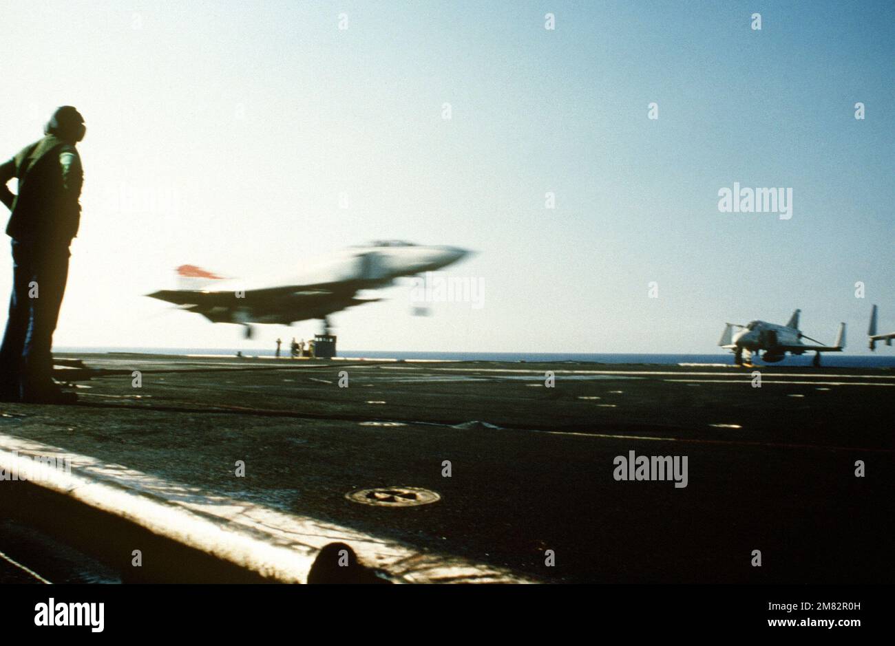 An arresting gear operator watches as an F-4S Phantom II aircraft comes ...