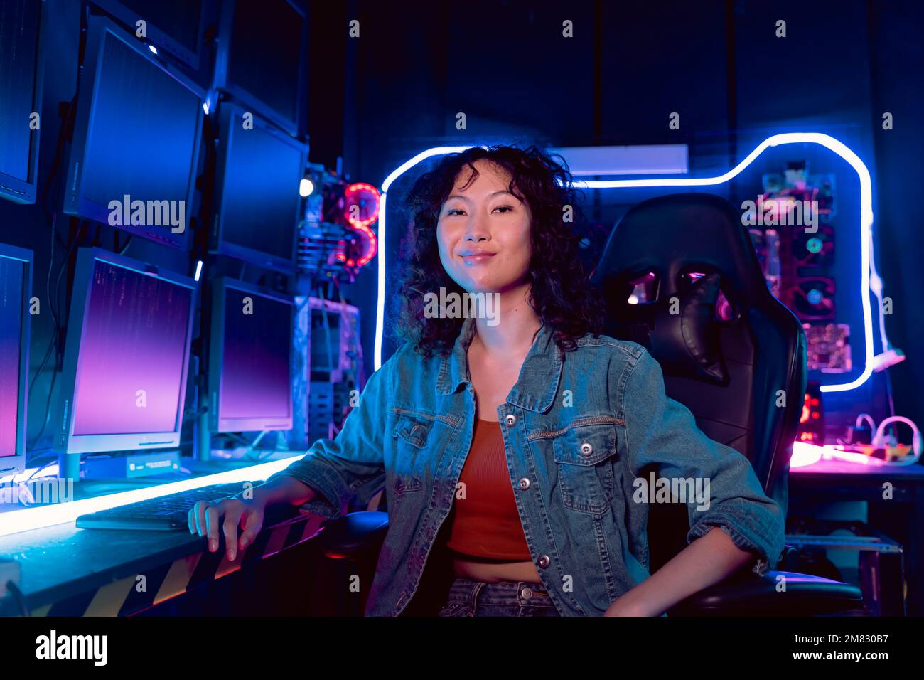 Female Asian hacker smiling in hideout place with dark environment and ...