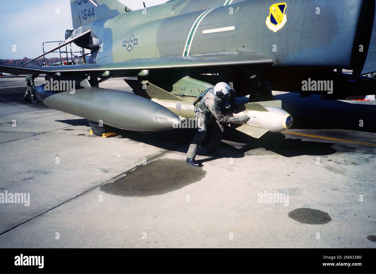 An air crewman inspects a GBU-15 bomb mounted on the wing of an F-4E ...