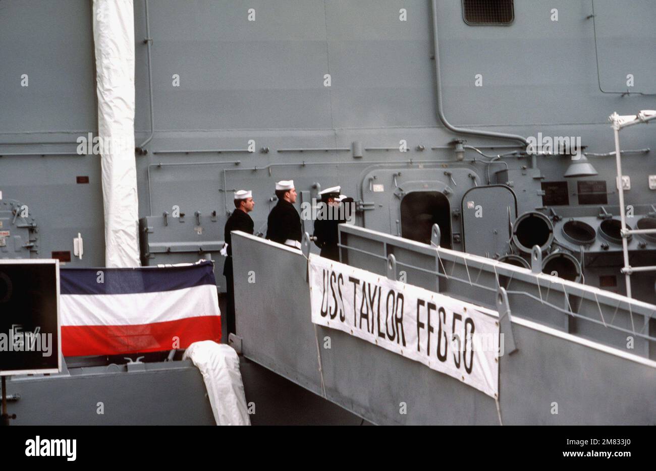 Three crewmen stand at attention on the quarterdeck of the guided ...