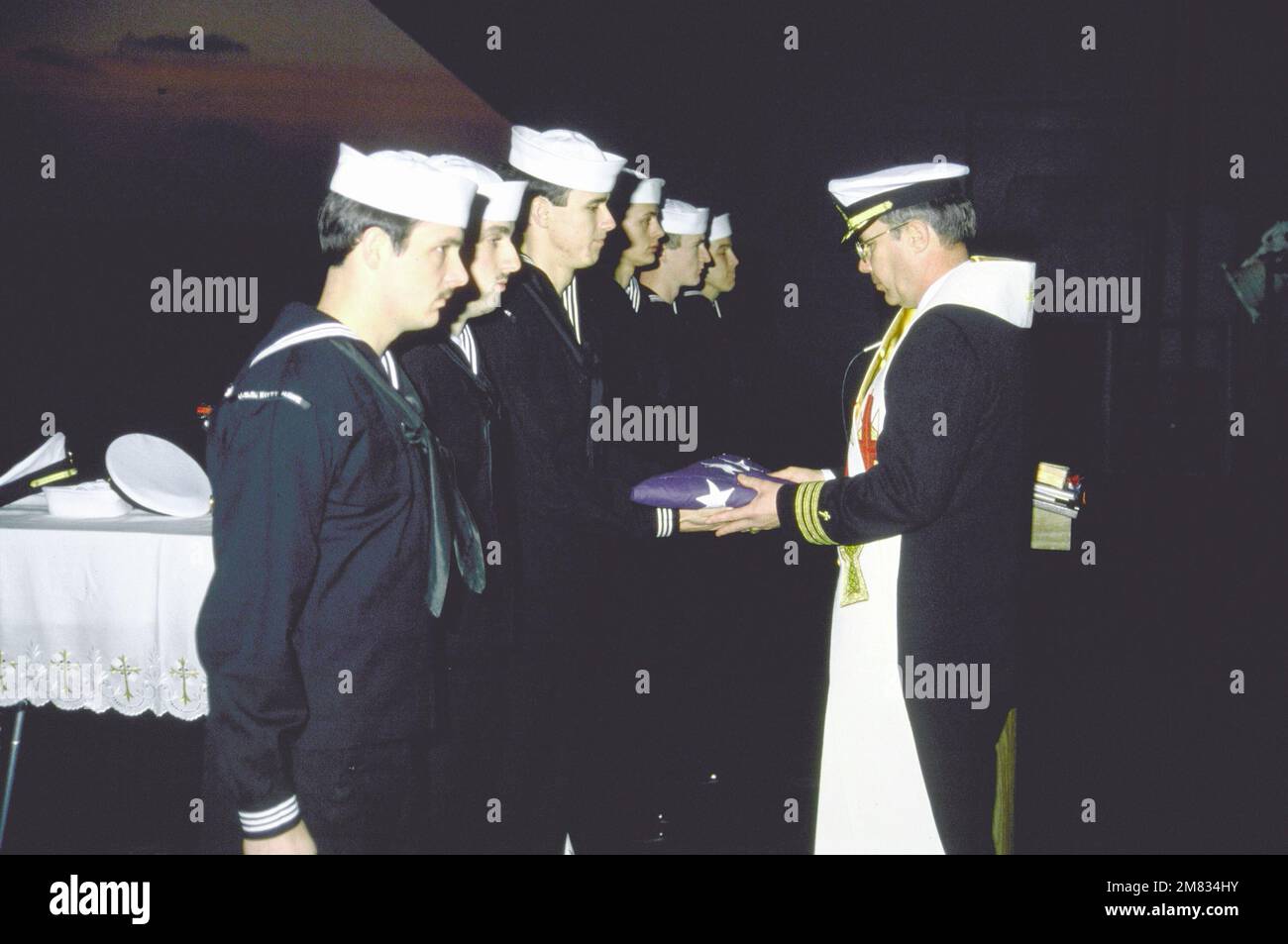 A chaplain presents the national ensign to a crewman following a burial ...