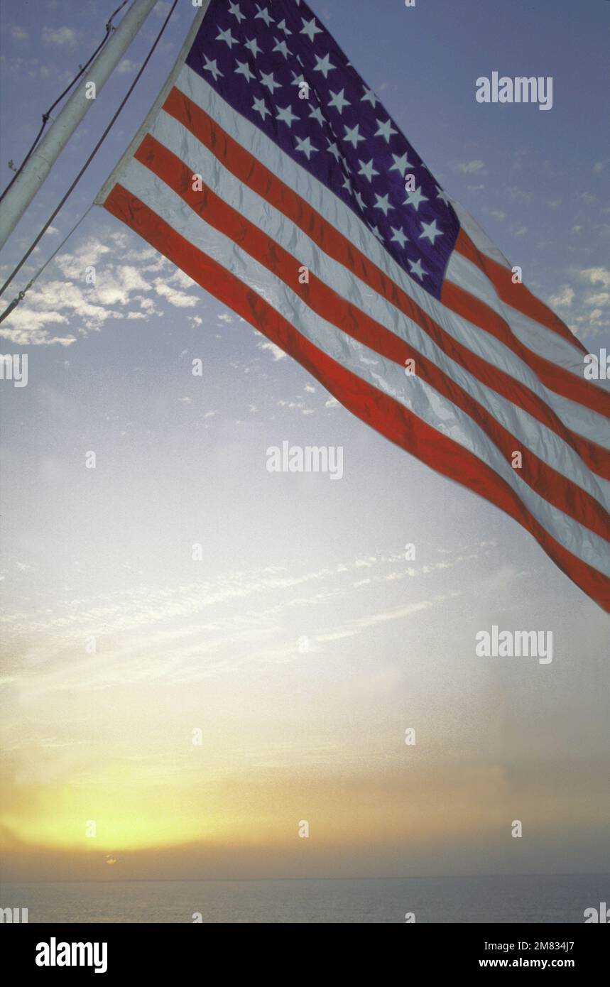 A sunset at sea provides the backdrop for the national ensign prior to ...