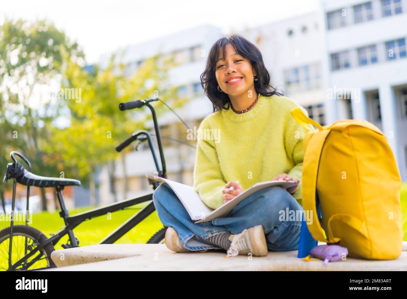 A young Asian female student making notes in the notebook sitting ...