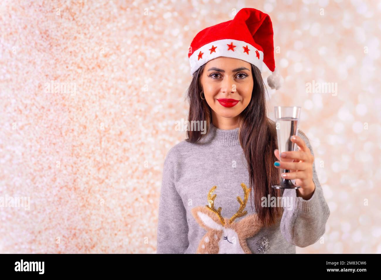 A Caucasian Brunette woman in Christmas sweater and hat holding glass ...