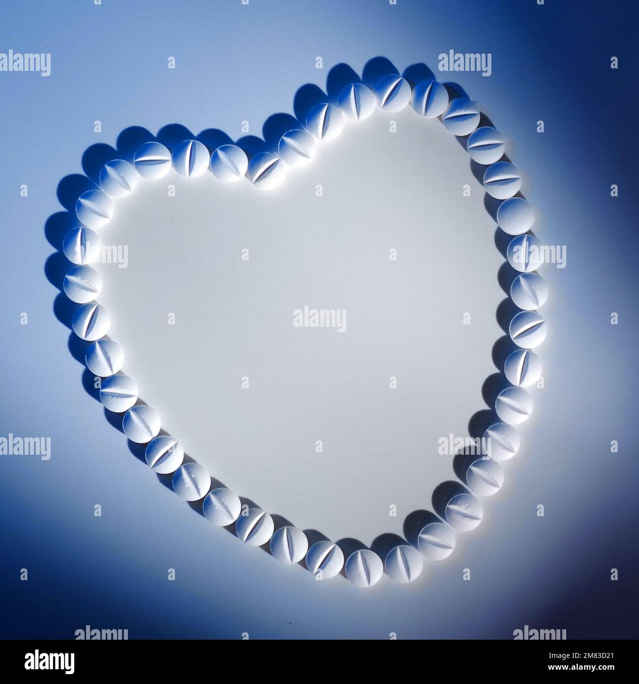Heart shape of white pills on light white background in blue hard light ...