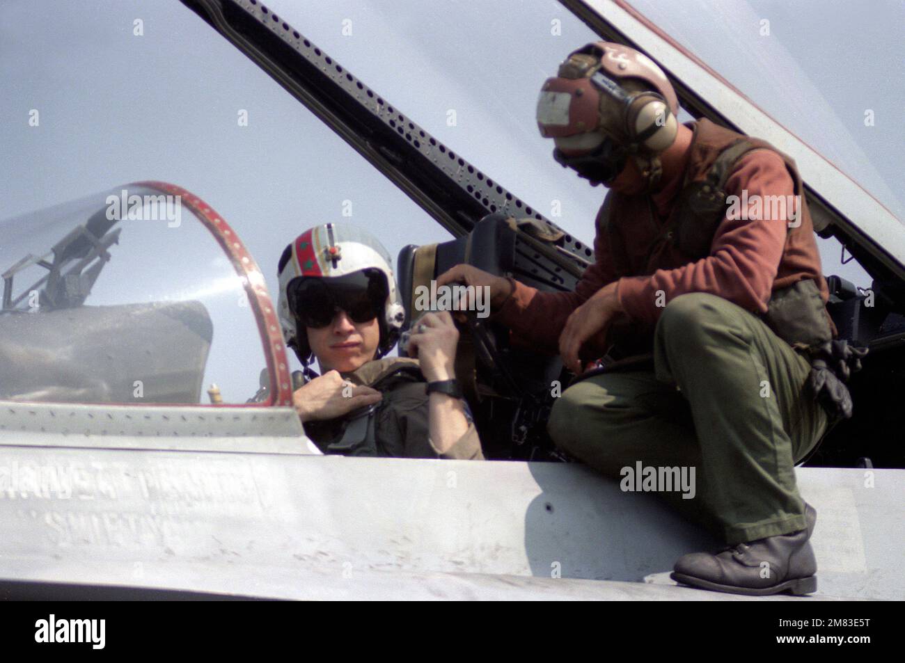 A crewman helps a pilot aboard an F/A-18 Hornet aircraft from Strike ...