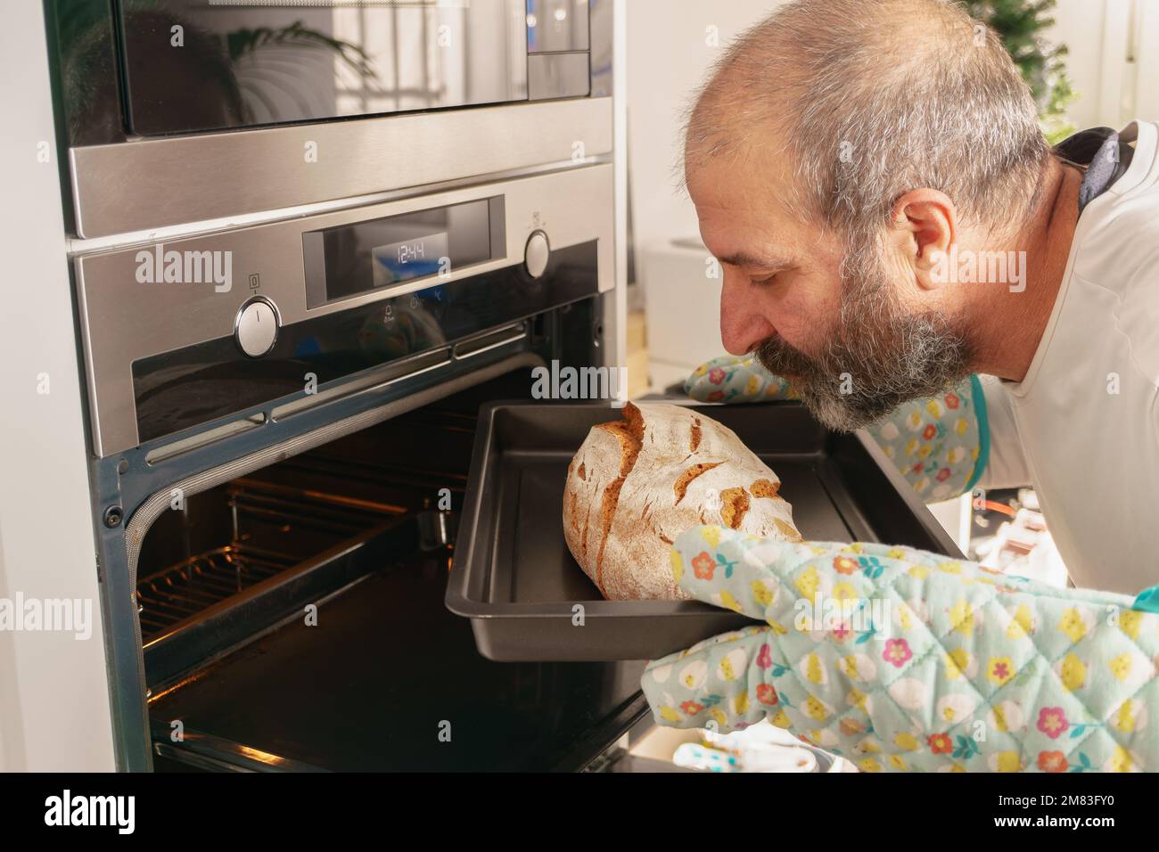 older man with beard putting bread in the oven of his house Stock Photo ...
