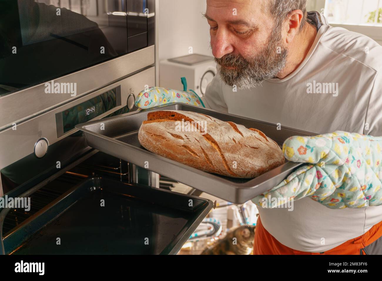 older man with beard putting bread in the oven of his house Stock Photo ...