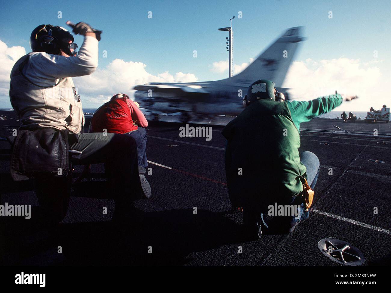 A catapult and arresting gear crewman gives hand signals as an A-7E ...