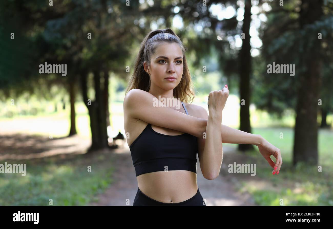 Beautiful woman stretches arms before training in park Stock Photo - Alamy