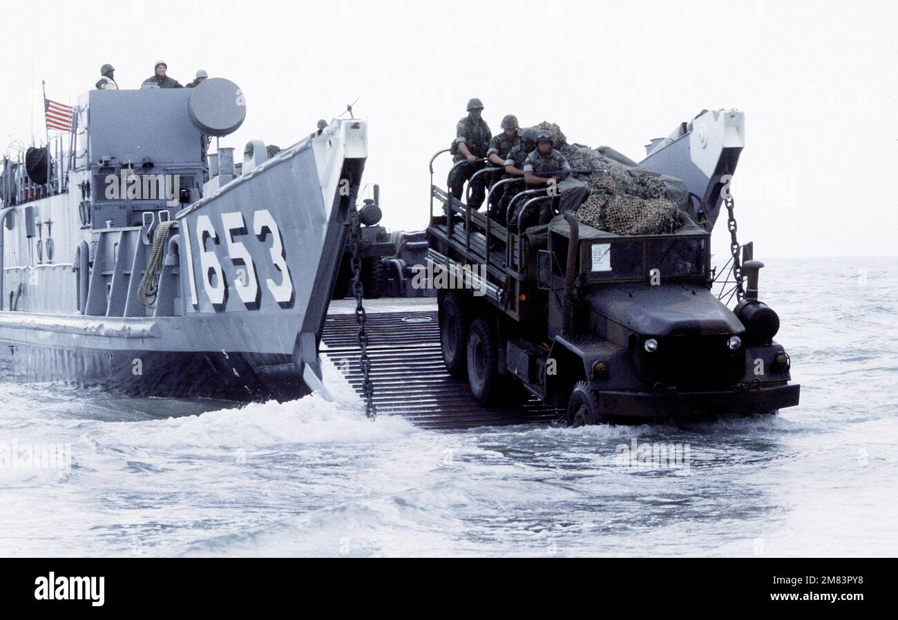An M-809 5-ton cargo truck is driven off the utility landing craft LCU ...