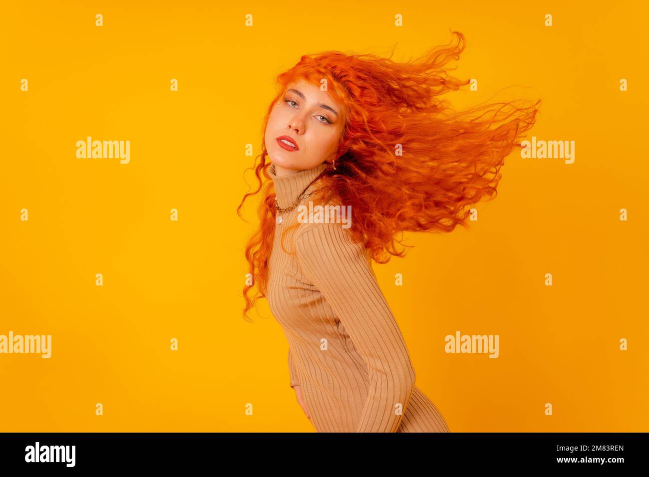 A red-haired Caucasian woman with tousled hair, posing on a yellow ...