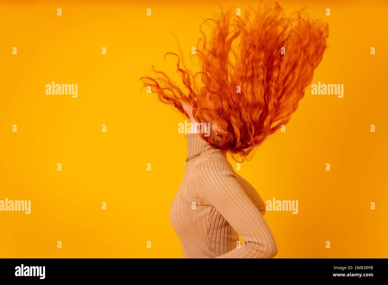 A red-haired Caucasian woman with tousled hair, posing on a yellow ...