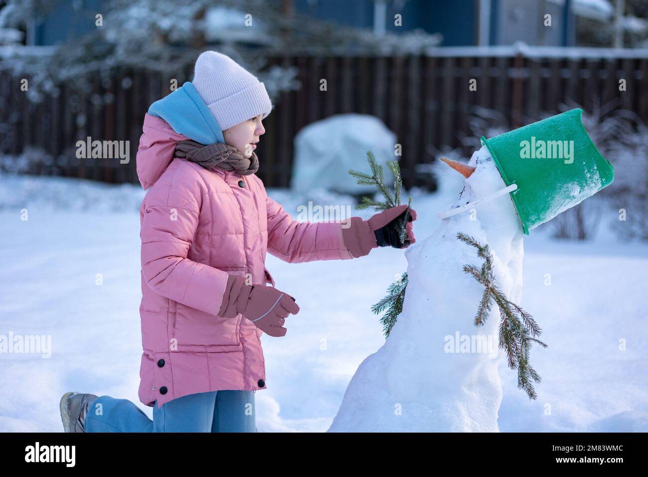 Little girl makes snowman on winter frosty day. Child makes hands from ...
