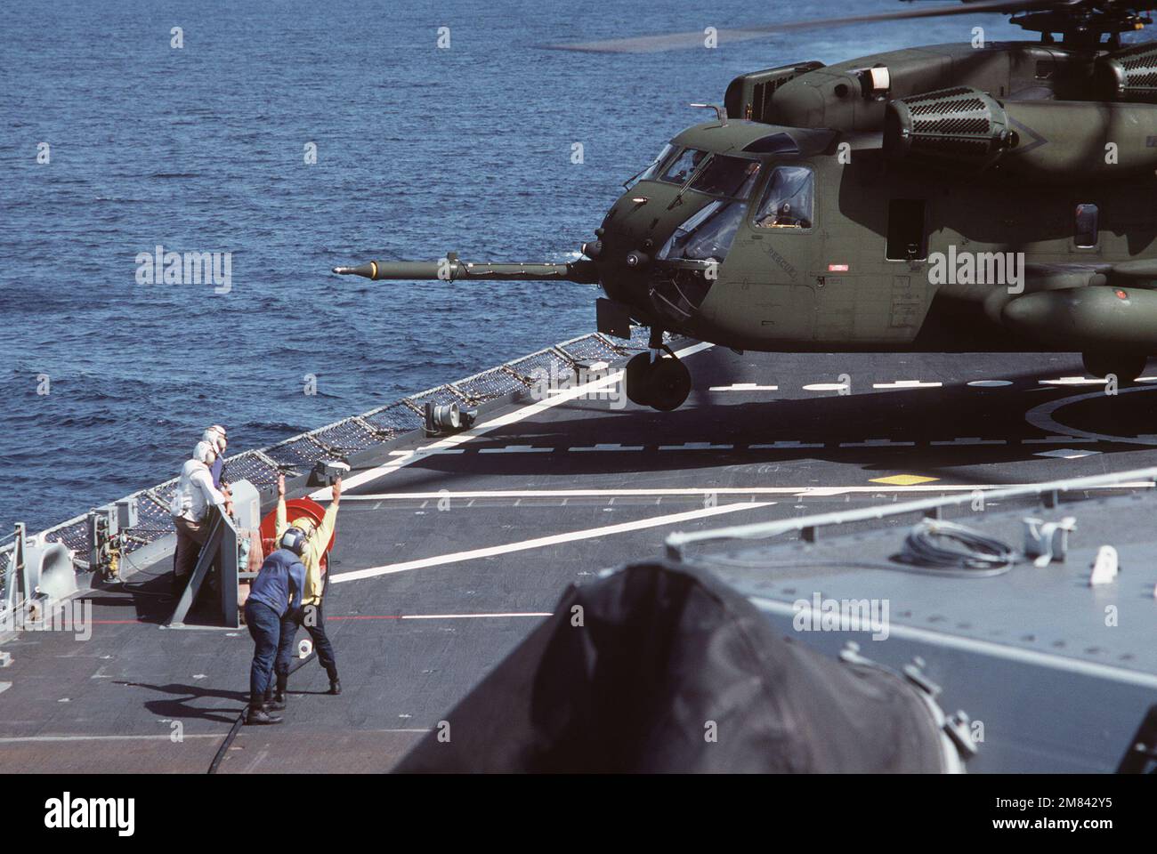 A flight deck crewmen signals to a CH-53E Super Stallion helicopter ...