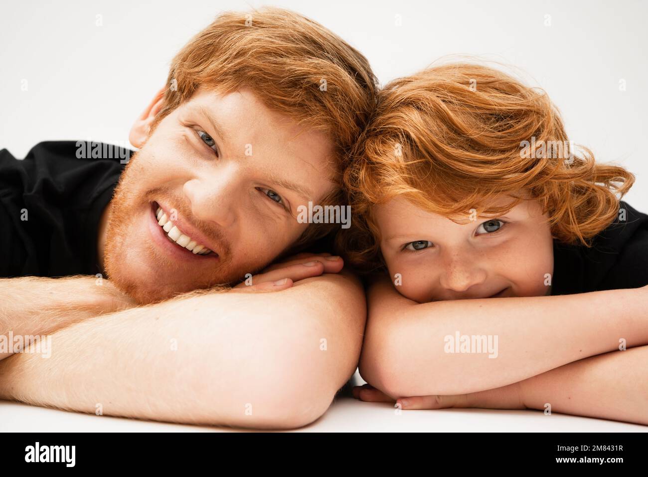 family portrait of redhead father and son lying with crossed arms and ...