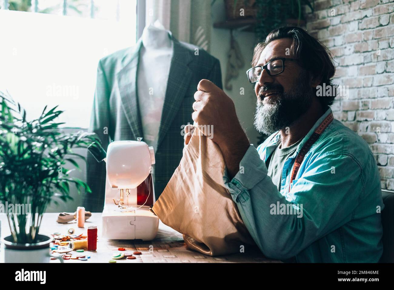 Happy worker in workshop. Tailor man using sewing machine alone and ...
