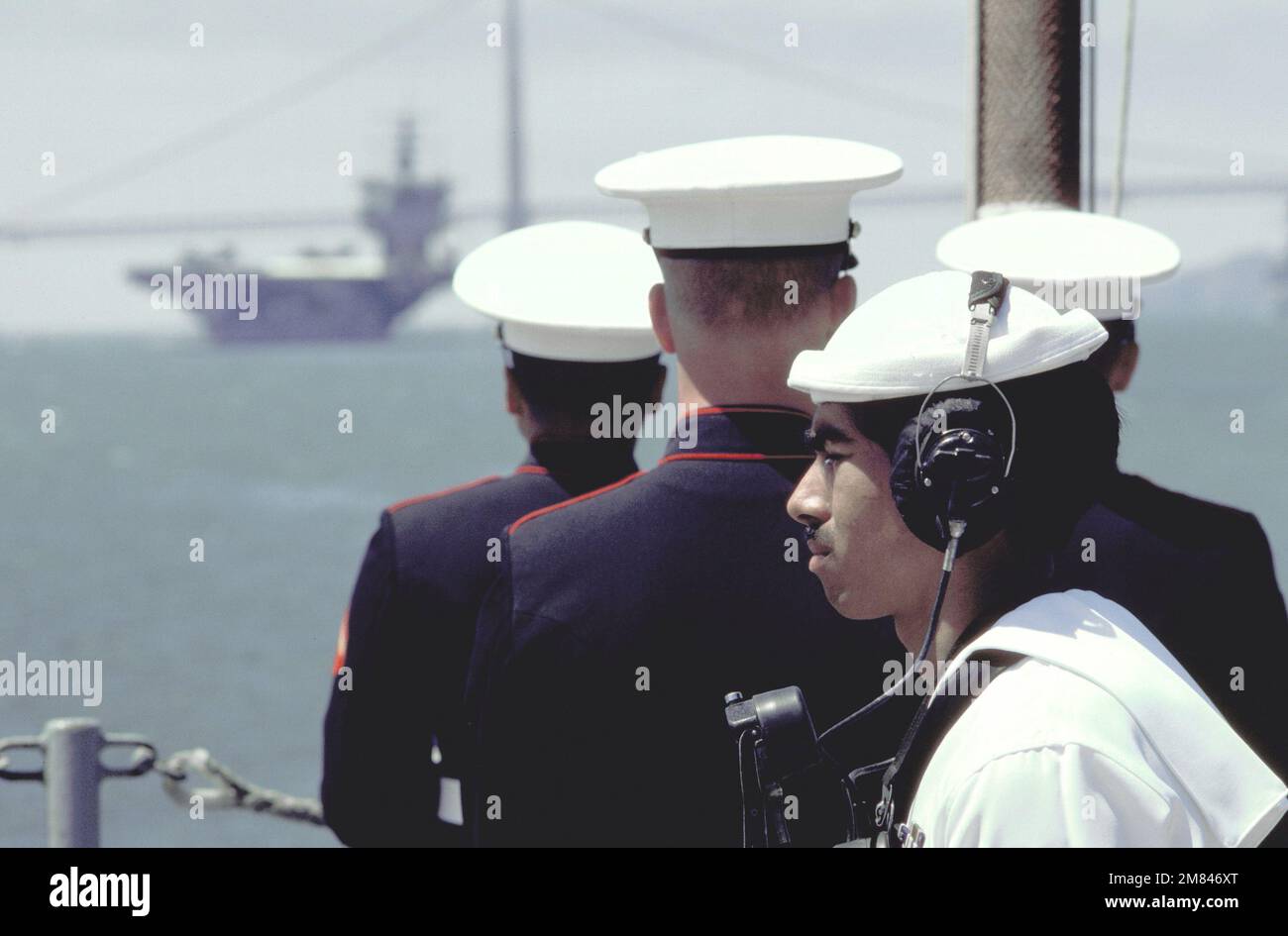 A sailor wearing a sound-powered telephone headset and members of a ...