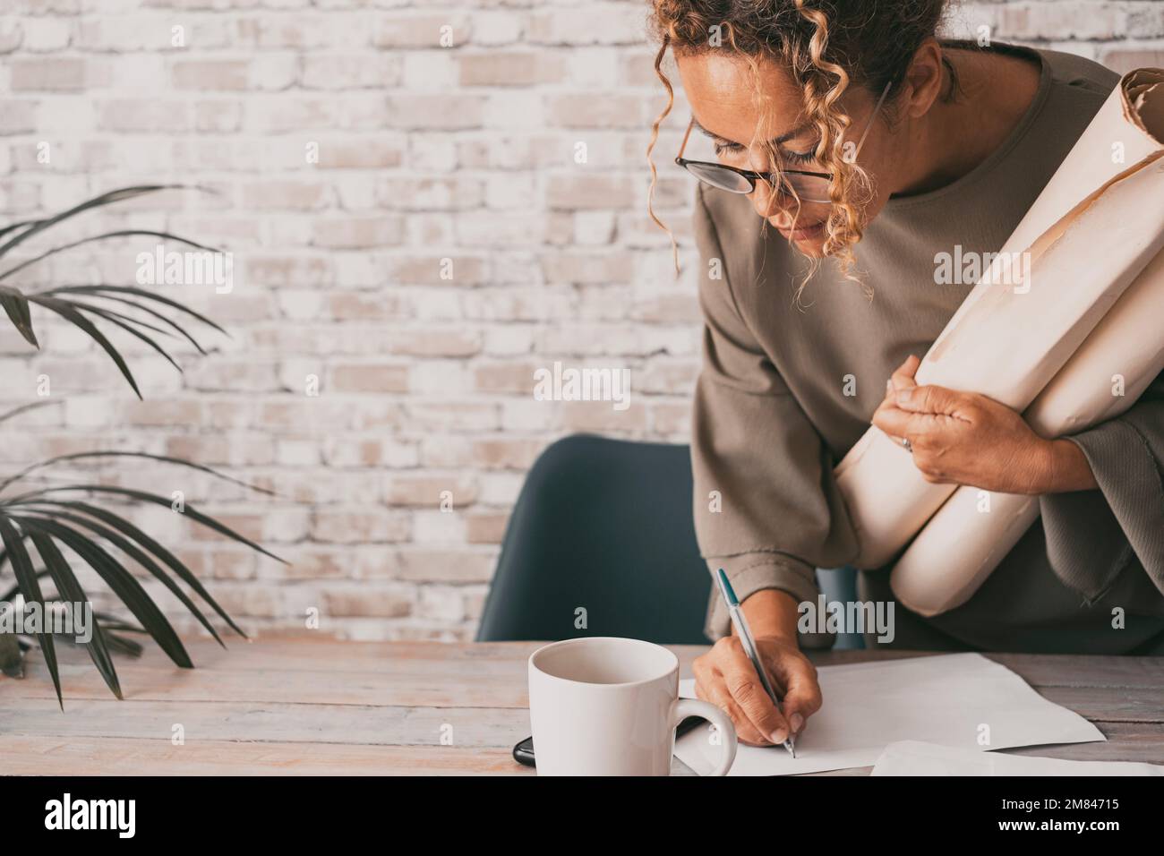 Businesswoman at work writing notes on sheet paper on the desk holding ...
