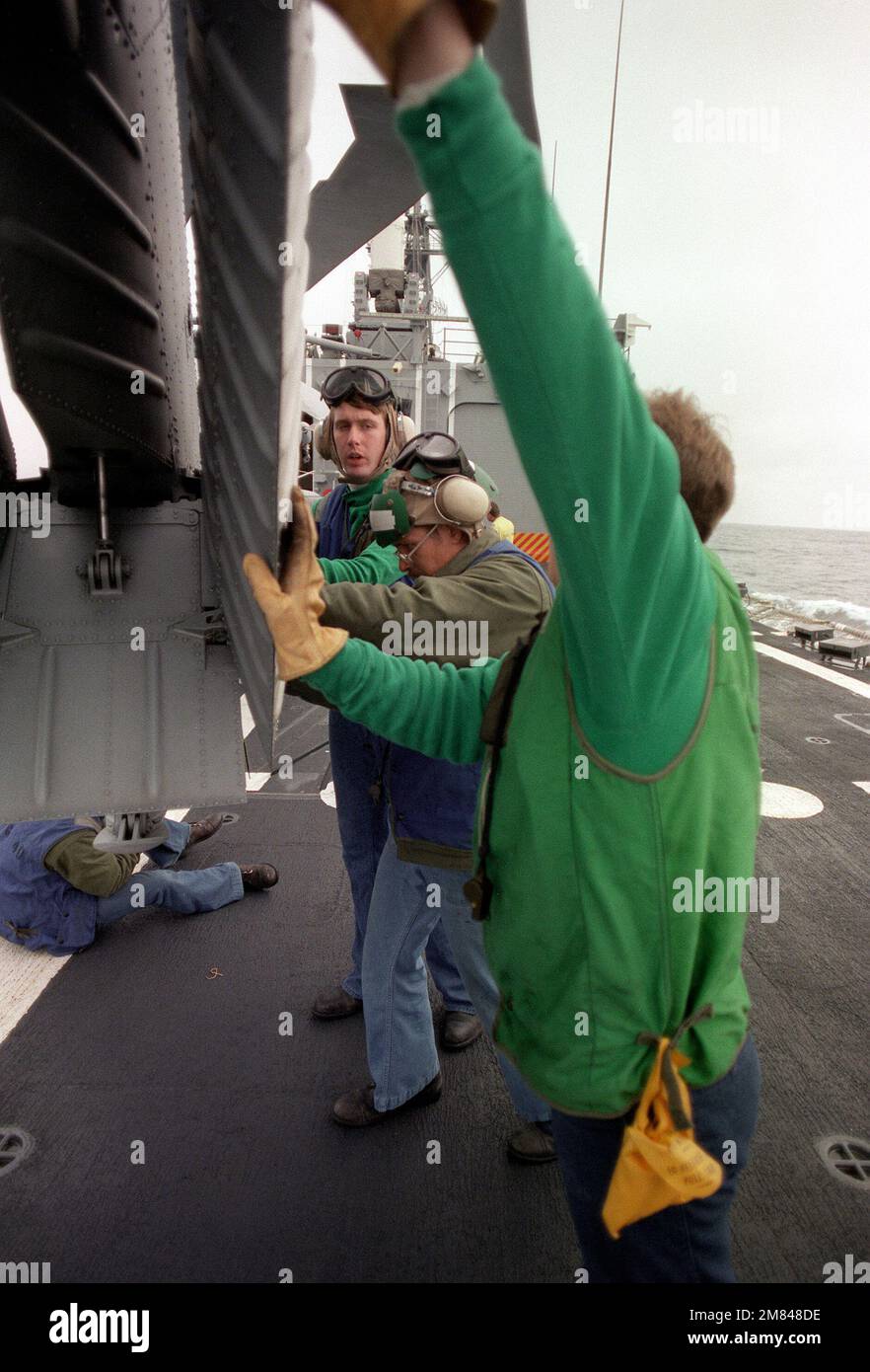 Crew members fold the tail section of an SH-60B Sea Hawk while the ...