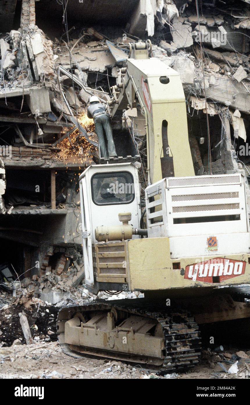 A Mexican rescue worker stands in the scoop of a backhoe while using a ...
