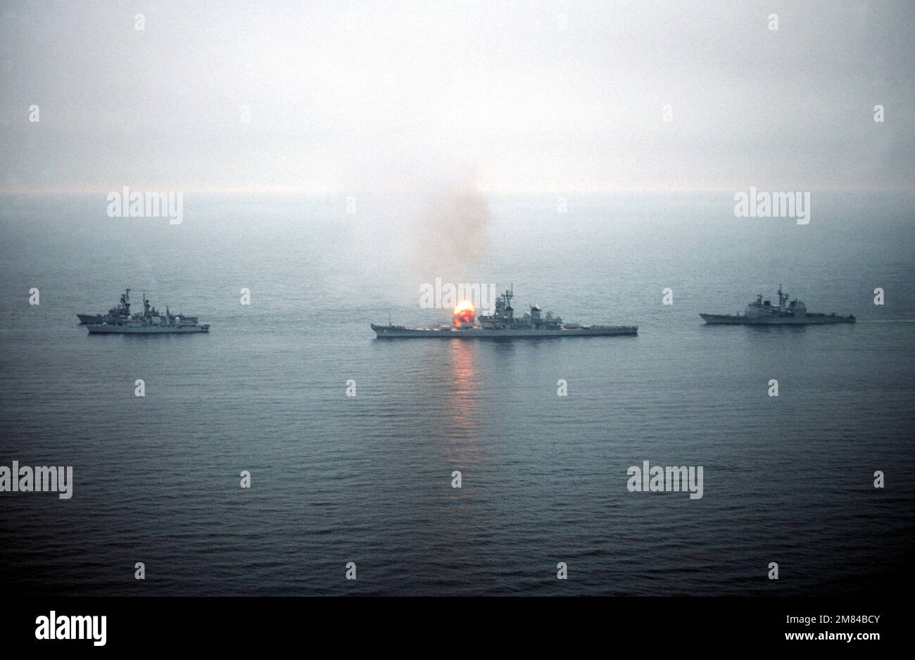 An elevated port beam view of the battleship IOWA (BB 61) firing a forward Mk 7 16 inch gun ...