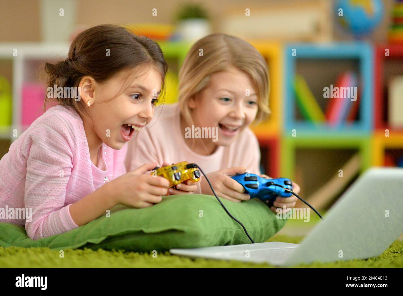 Two pretty little girls lying playing video game Stock Photo - Alamy