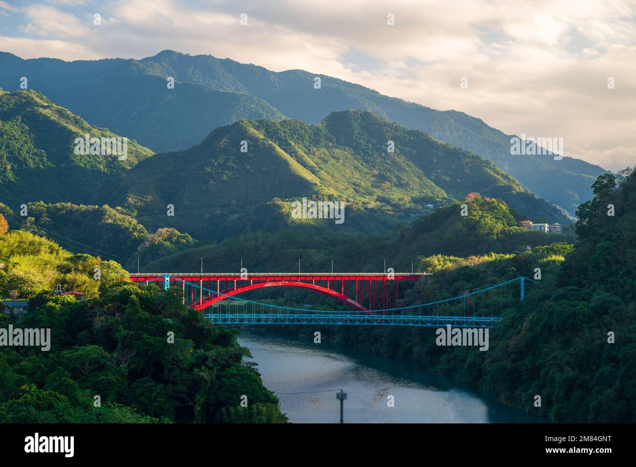 The beautiful red bridge over the stream. The sun shines on the green ...
