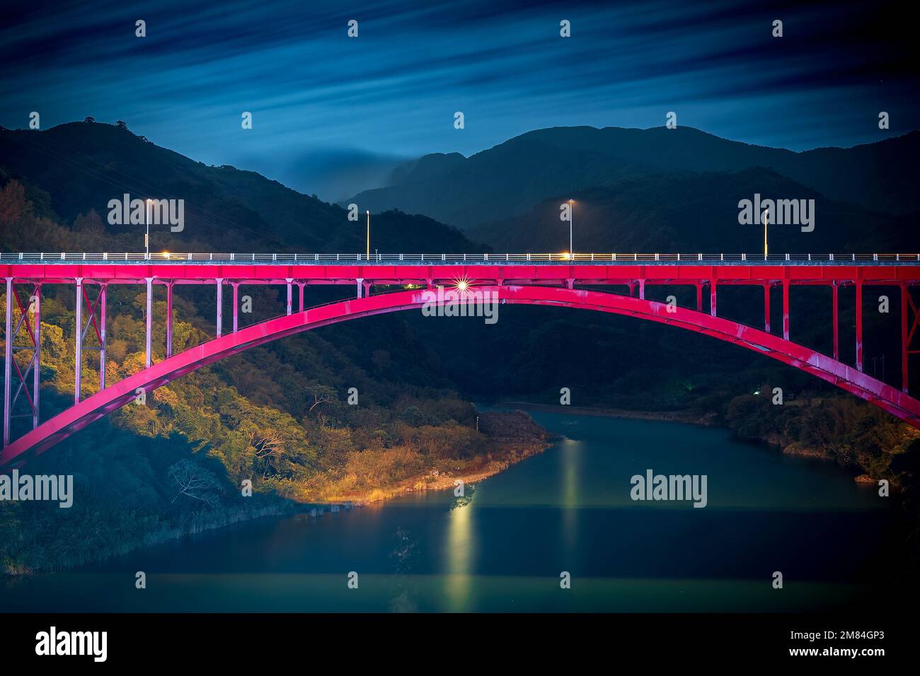 The beautiful red bridge over the stream. The sun shines on the green ...