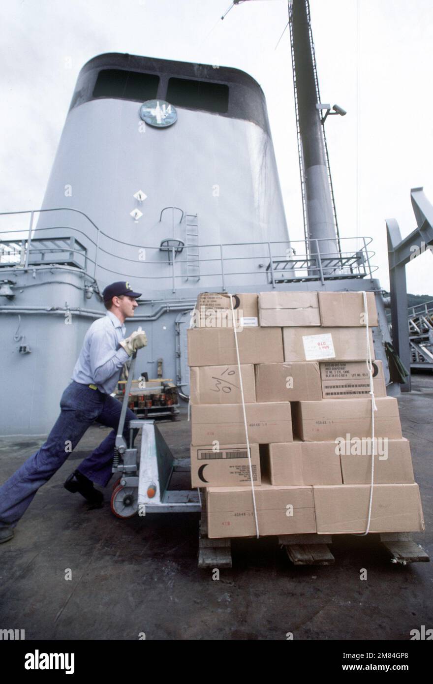 A sailor pushes a pallet of supplies across the deck of a ship at Navy ...