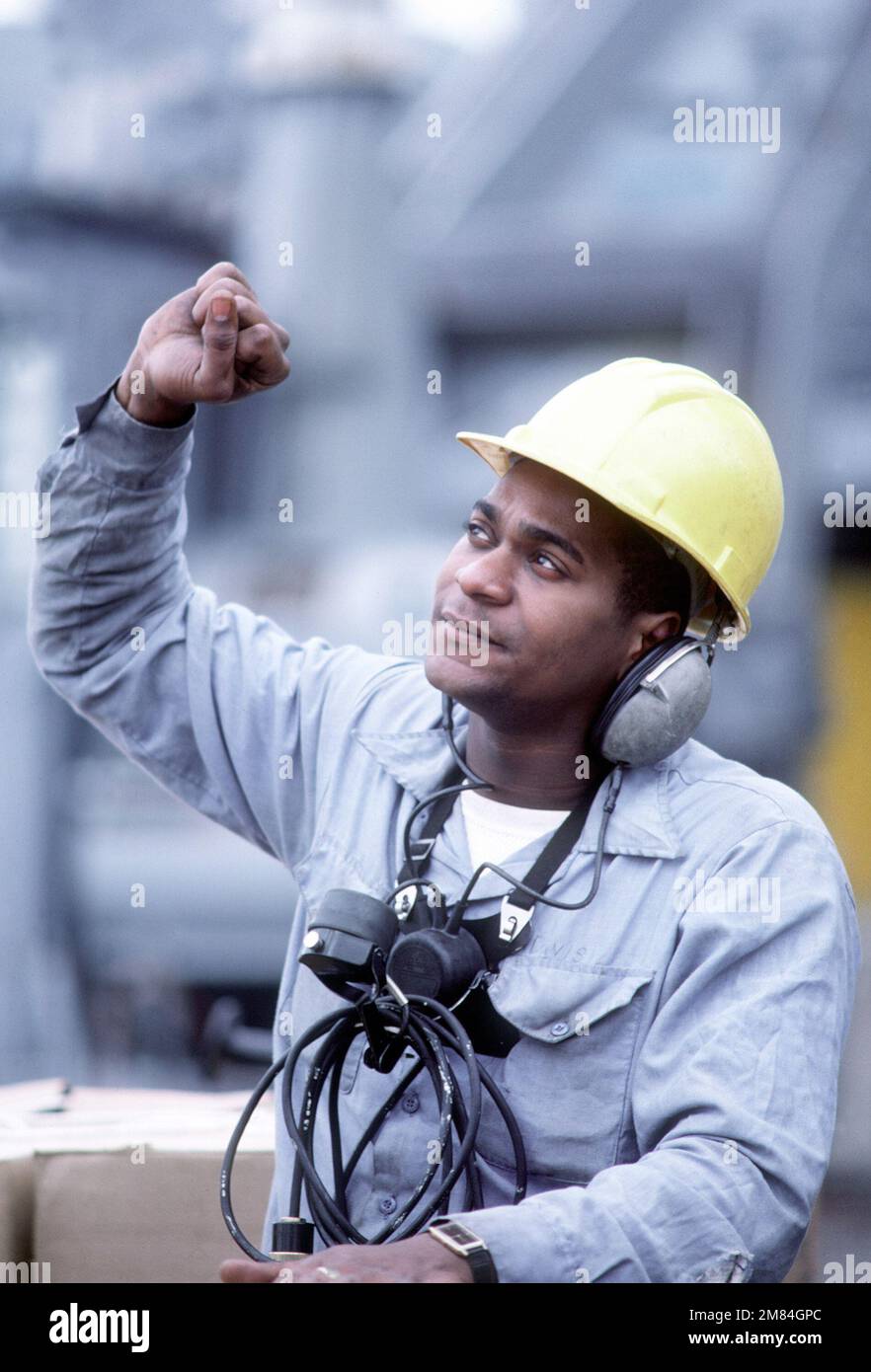 A sailor wearing a sound powered headset signals directions while ...
