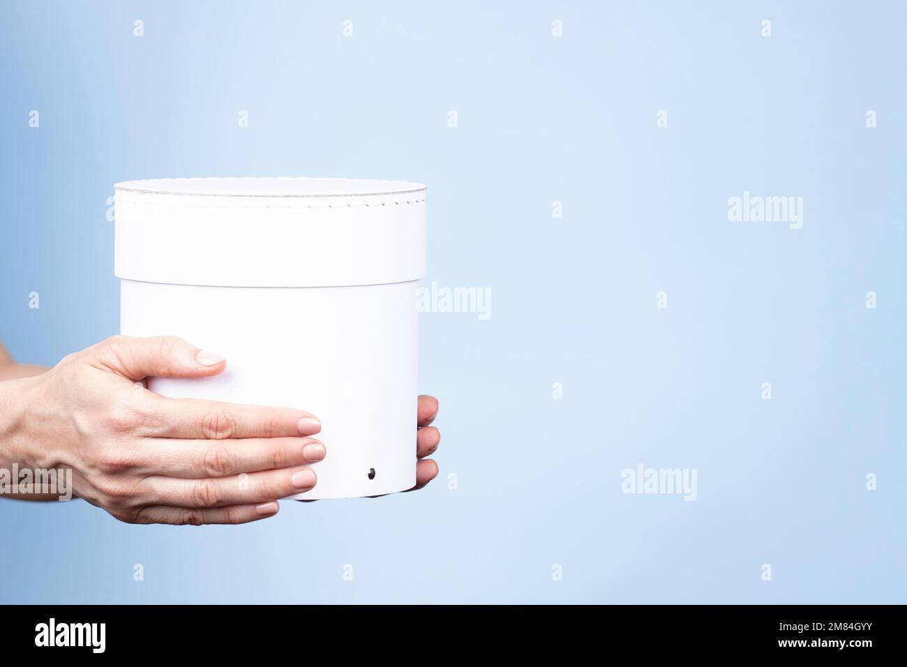 Woman hands holding white round cardboard box with cap on light blue ...