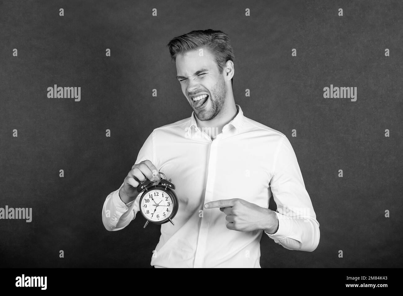 Happy crazy guy sticking tongue while pointing finger at alarm clock ...
