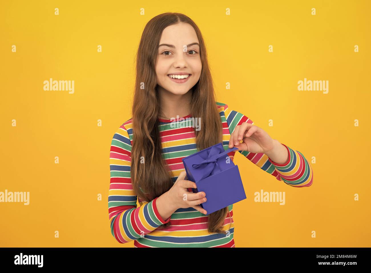 Young teenager girl child holding gift box isolated on yellow ...