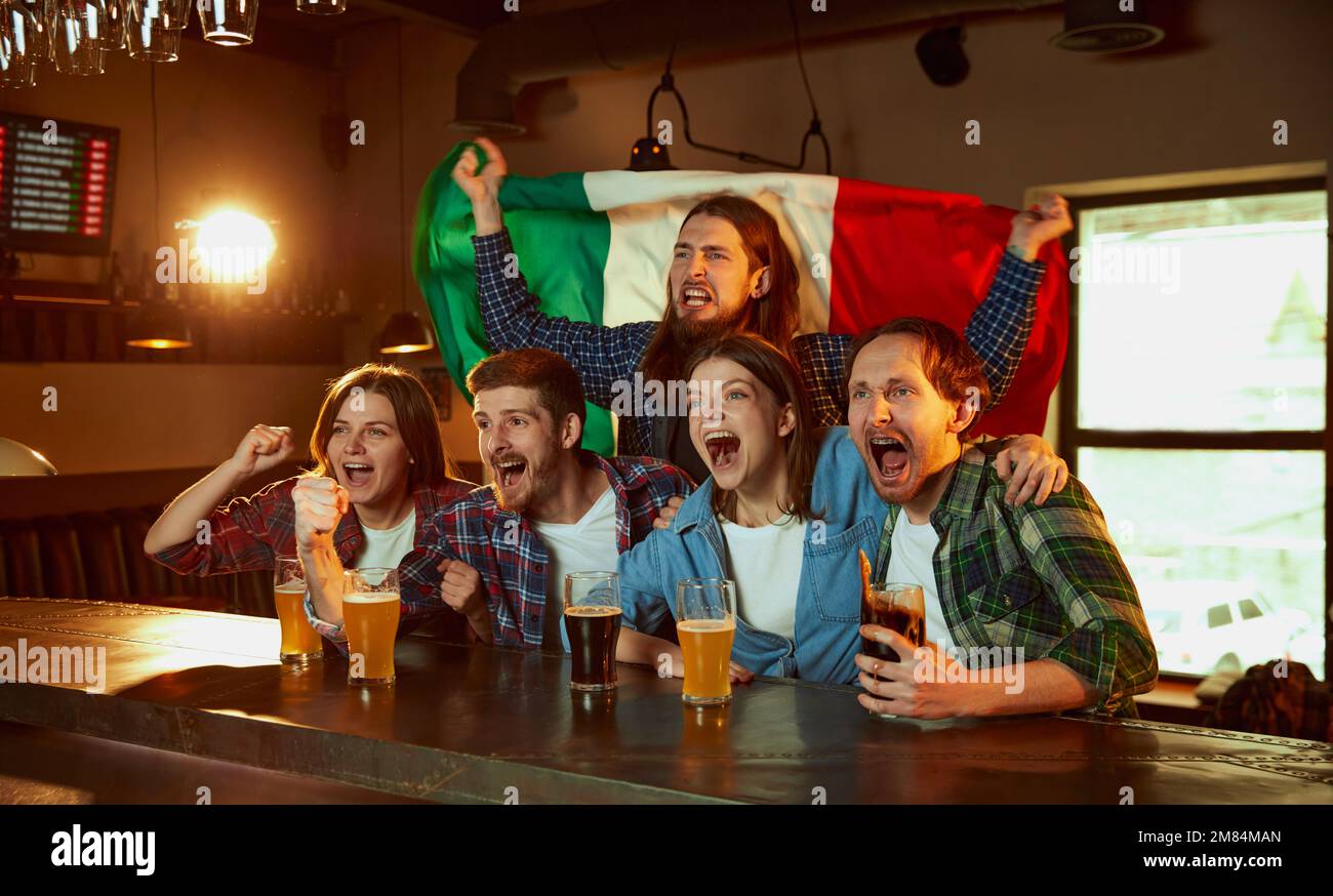 Group of young people, men and women watching match at pub. Fans ...