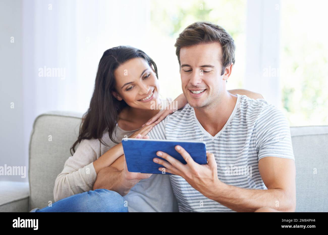 Showing her his new tablet. A young couple sitting on a couch using a ...