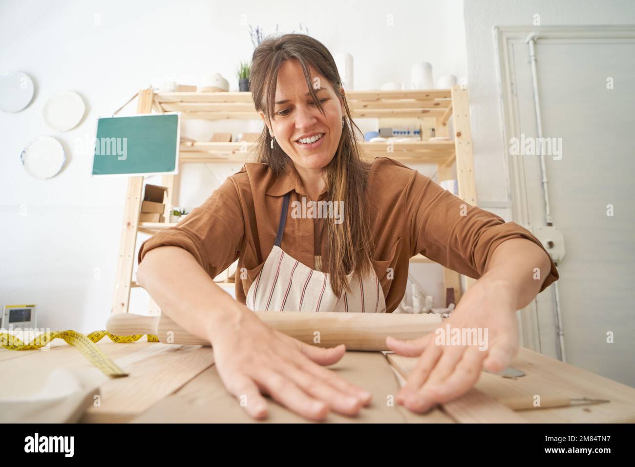 Female potter's hands roll out clay on the table with a wooden rolling ...