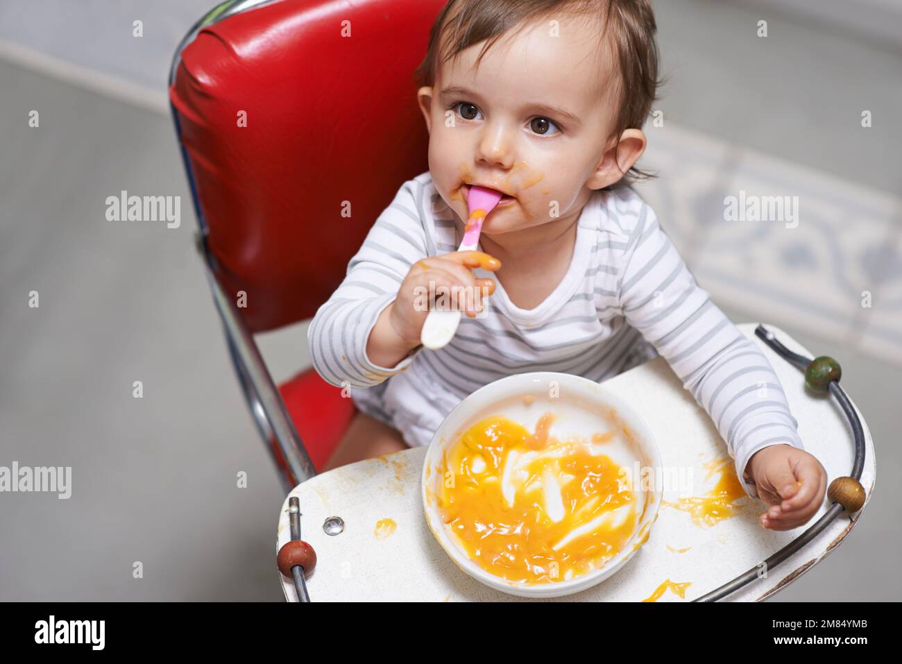 Exploring new tastes. A cute little baby sitting in a highchair eating ...