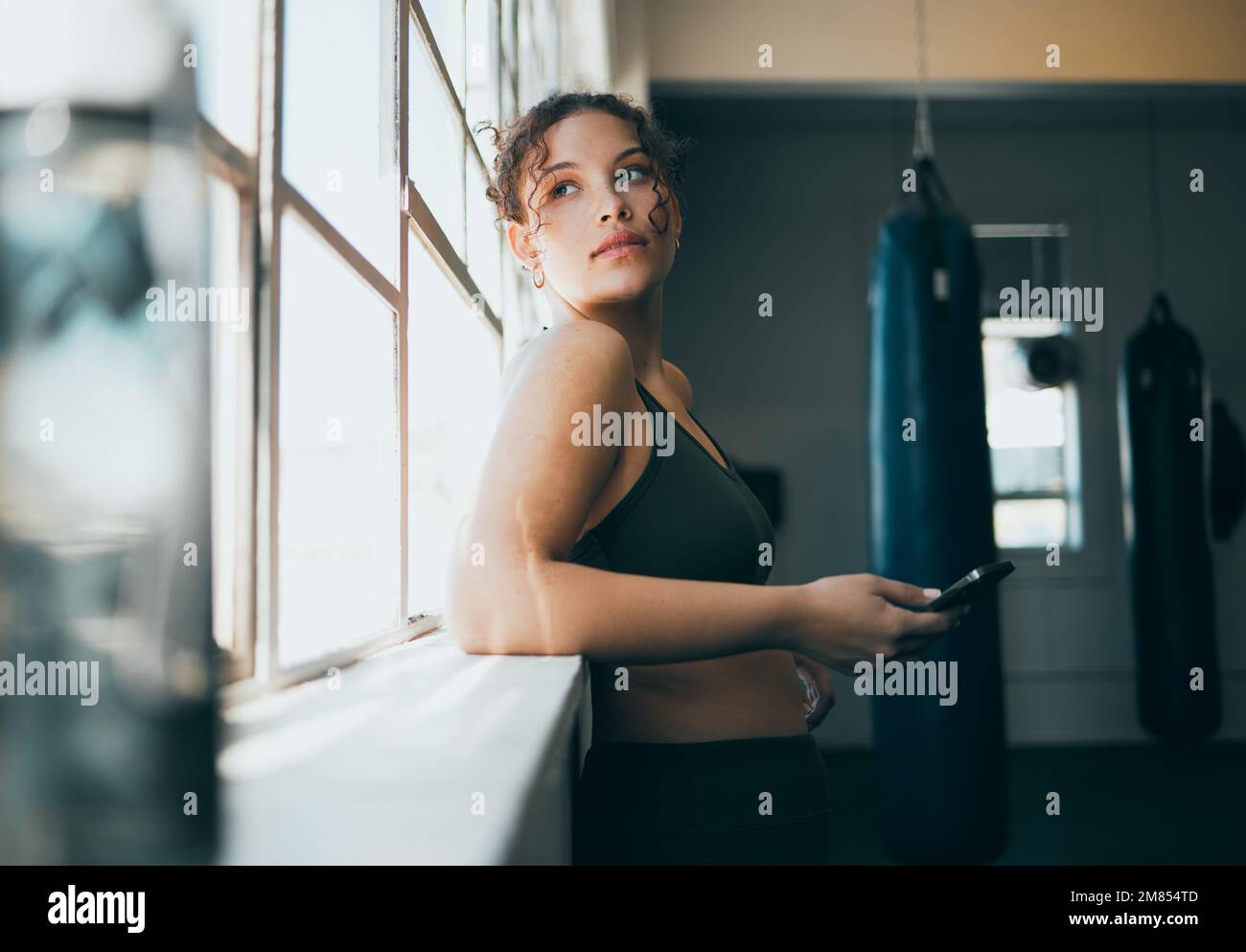 Thinking, phone and fitness with a sports woman by a window, standing ...