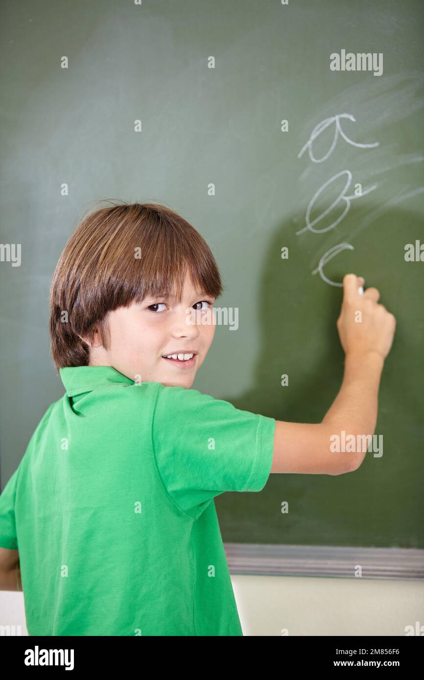 Practicing his cursive writing. A little boy writing on the blackboard ...