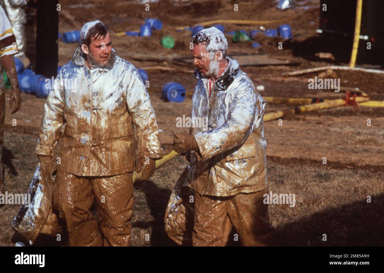 Mud and foam-spattered firefighters in a proximity suit take a break ...