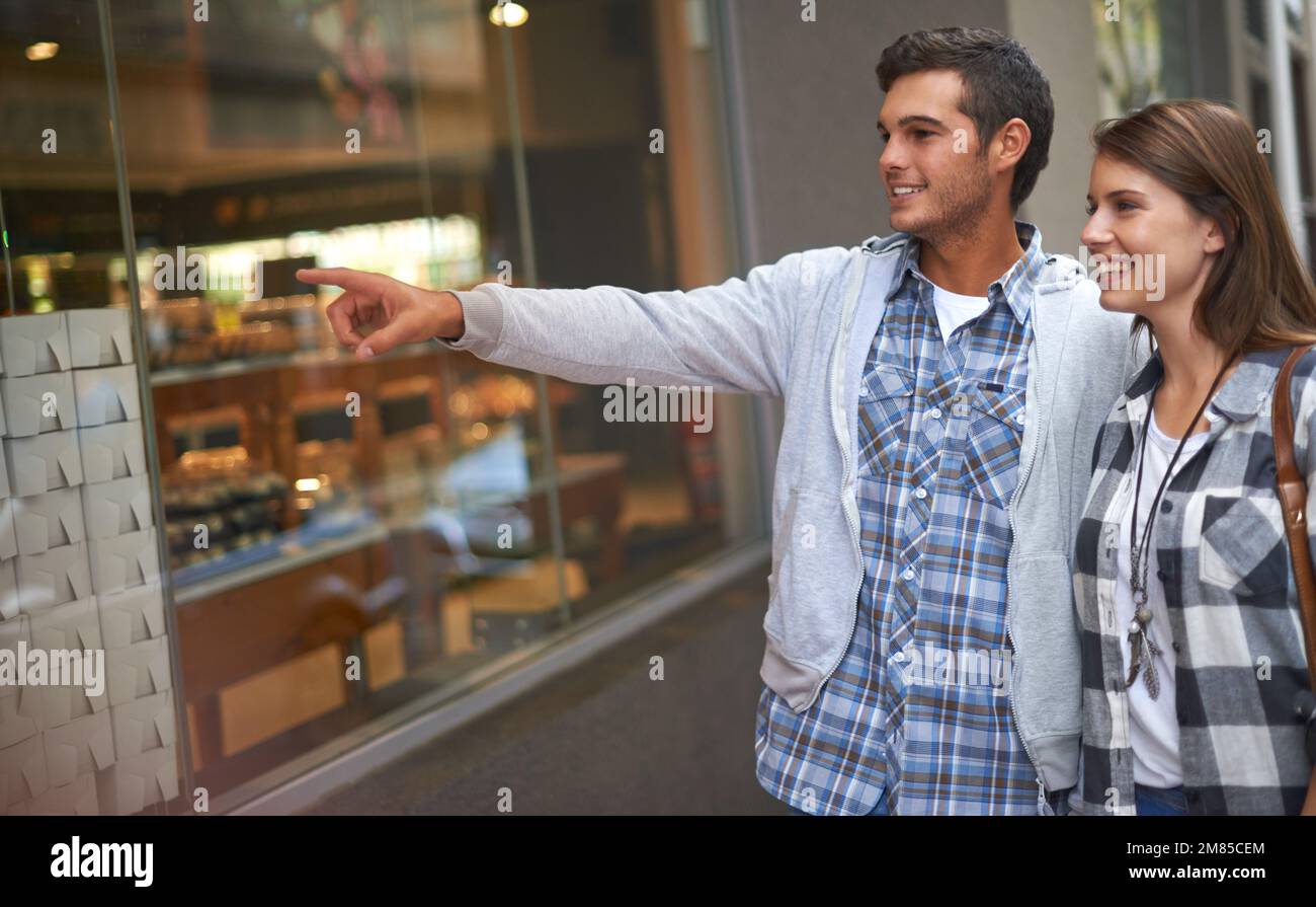 I want a cupcake. A young couple pointing at cakes through a bakerys ...