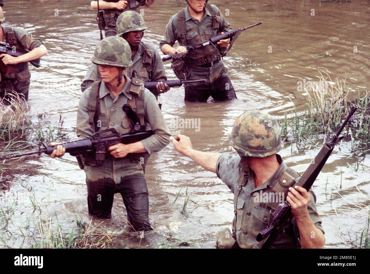 U.S. Army soldiers armed with M-16A1 rifles wade across a stream during ...