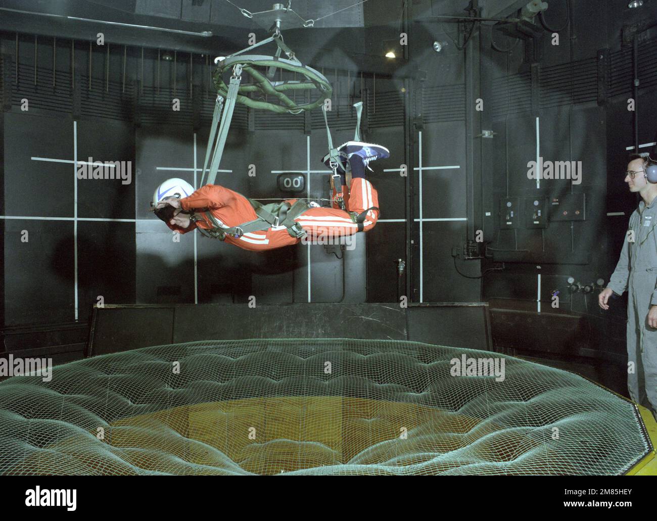 Technicians assist a test subject into a harness prior to a simulated ...