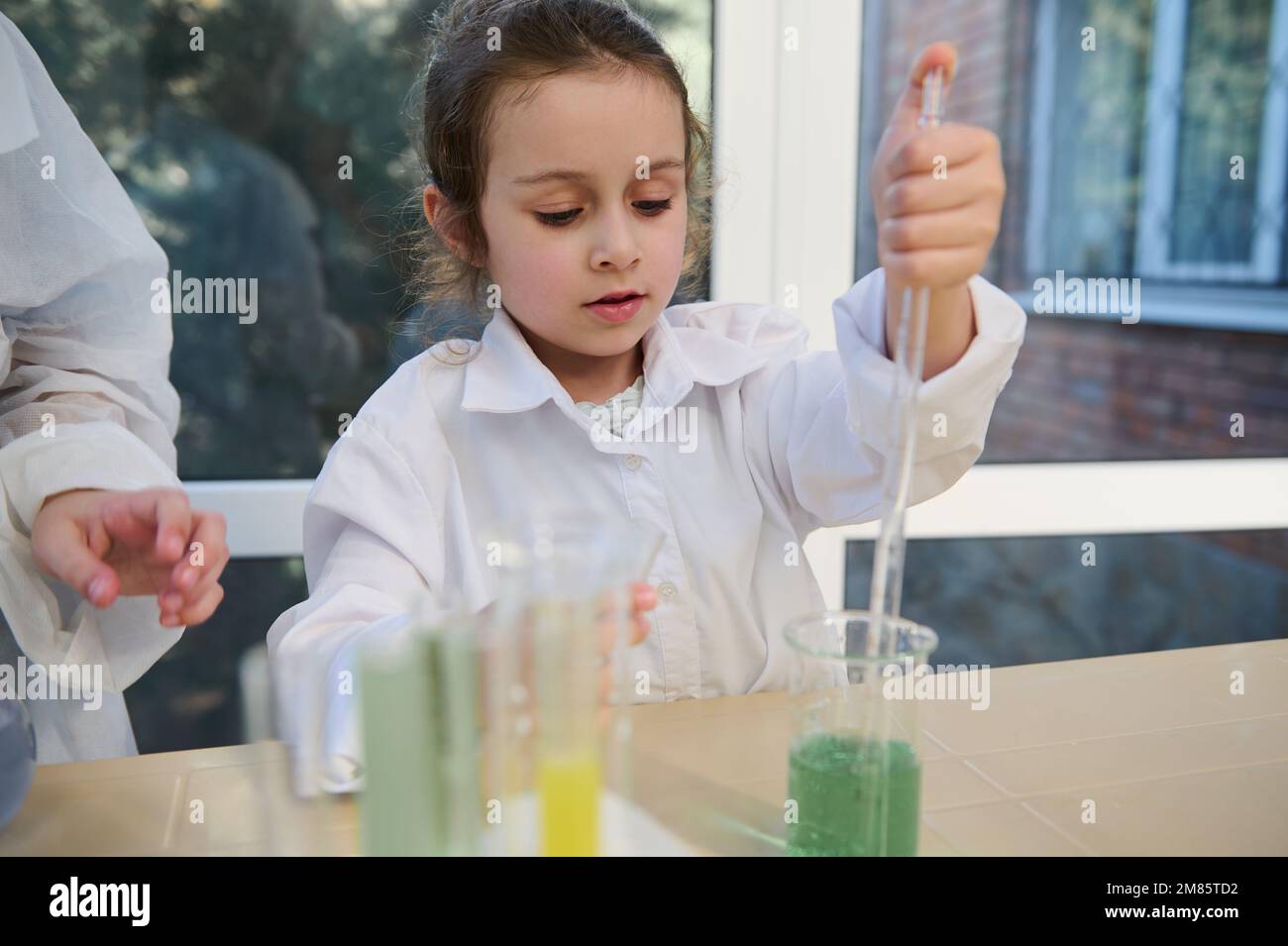 Adorable smart schoolkid using graduated pipette, dripping few reagents ...