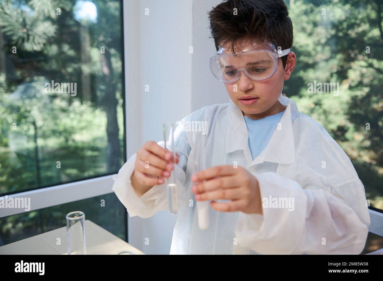 Teen schoolboy wearing white lab coat, holding test tubes with ...