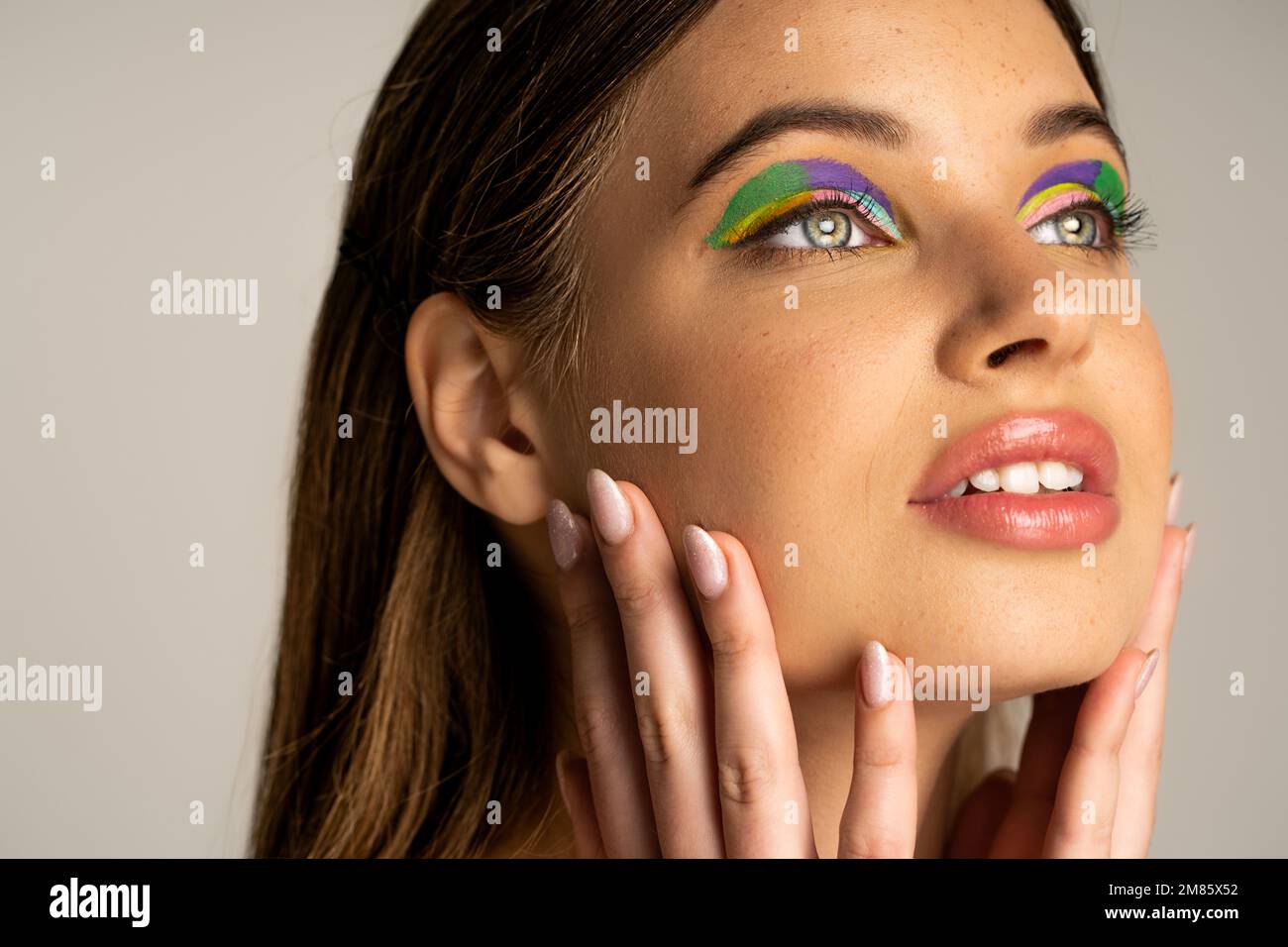 Teenage model with colorful visage touching face and looking away ...