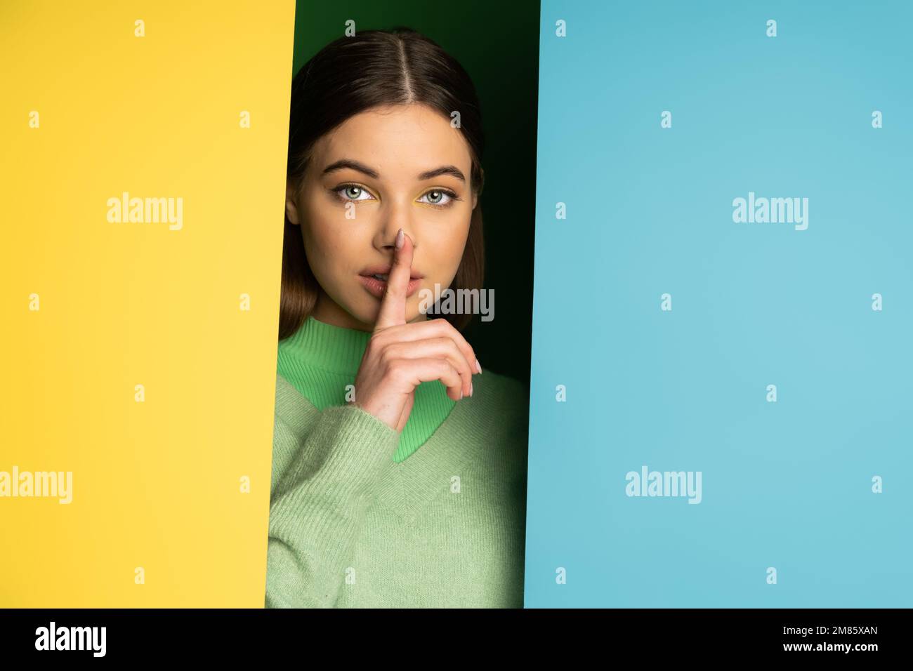 Brunette teen girl in jumper showing secret gesture on colorful ...